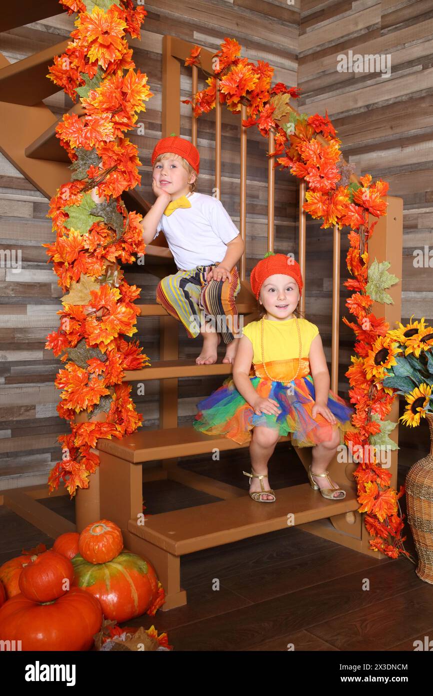Little boy and girl in pumpkin costumes sitting on the stairs with ...