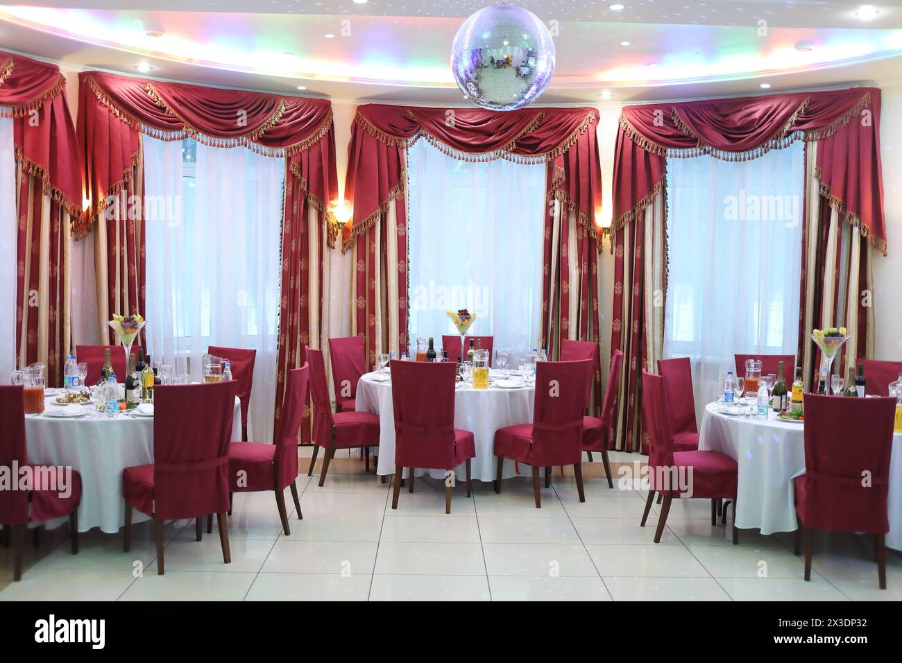 Beautiful banquet hall with round served tables, red chairs and drapes ...