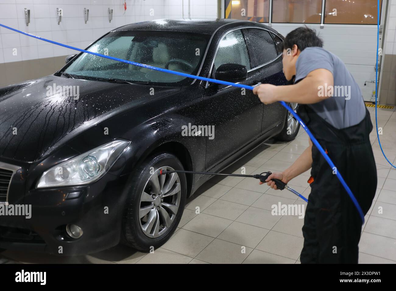 A car washman with a high-pressure cleaner washing wheel of a black car ...