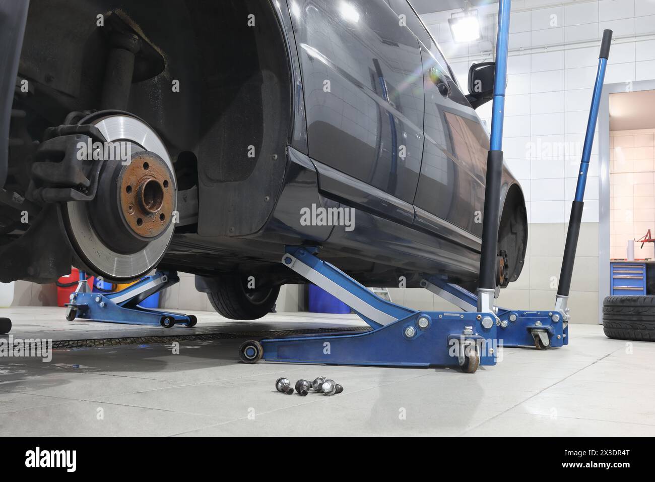 Hydraulic floor jacks under a black car without a wheel in the car ...