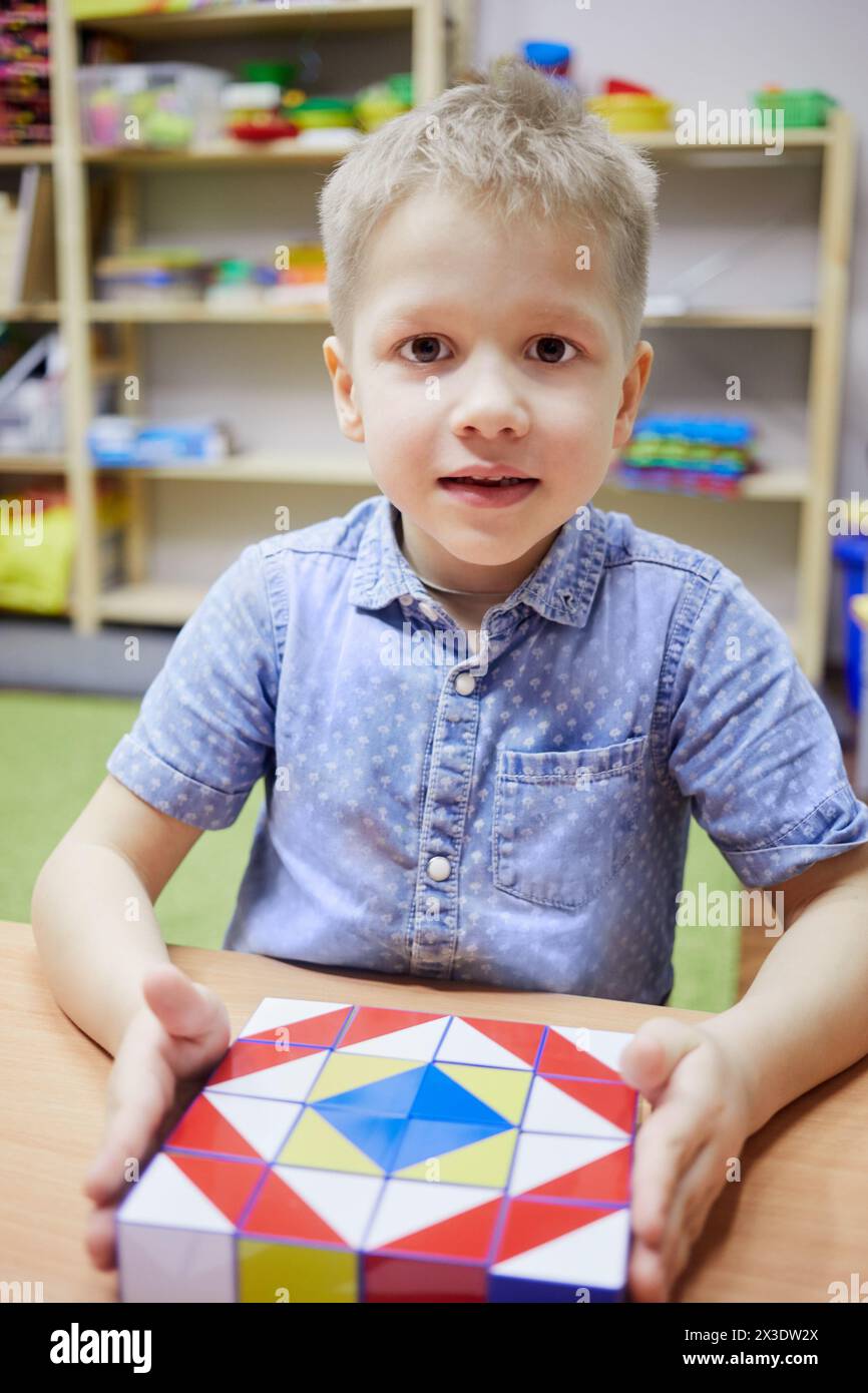 Little boy sits at desk with set of puzzle blocks in classroom at ...