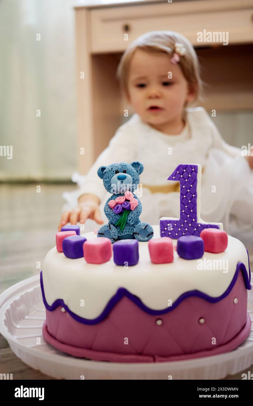 Little girl in white dress stretches arm to birthday cake decorated ...