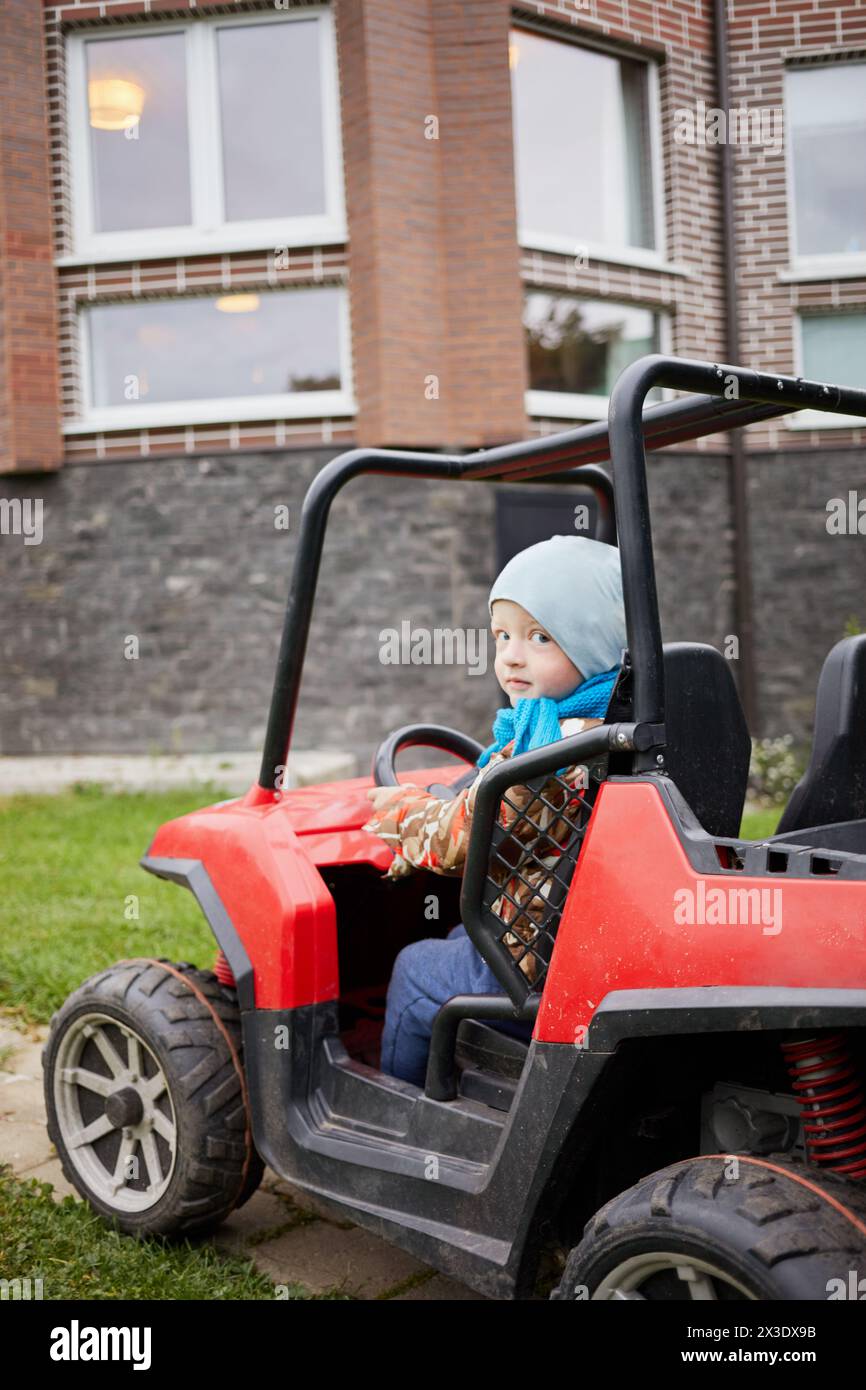 Little boy sits in children car at yard in front of brick cottage Stock ...