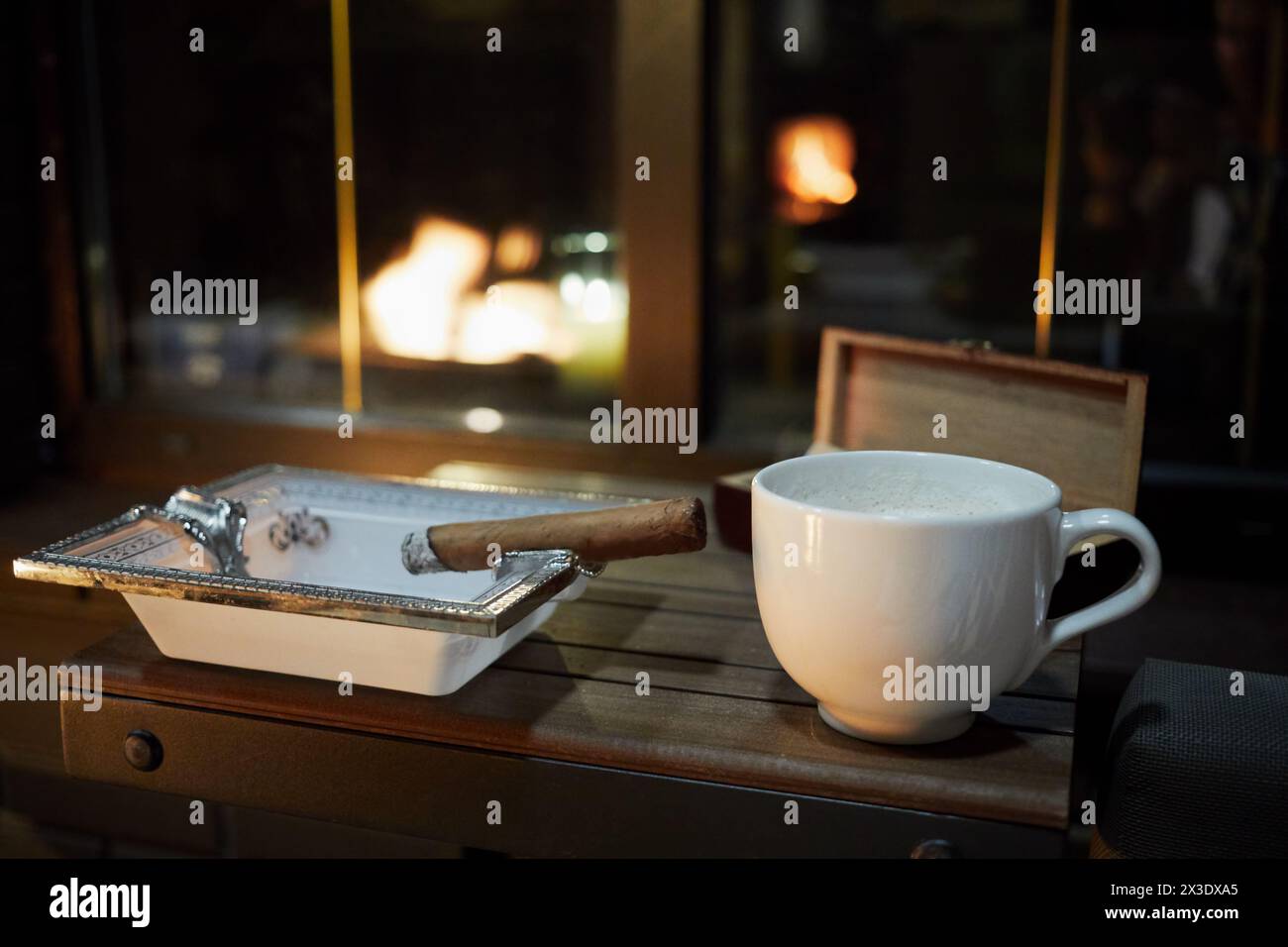 White cup of coffee, burning cigar on ashtray on wooden cigar table on ...