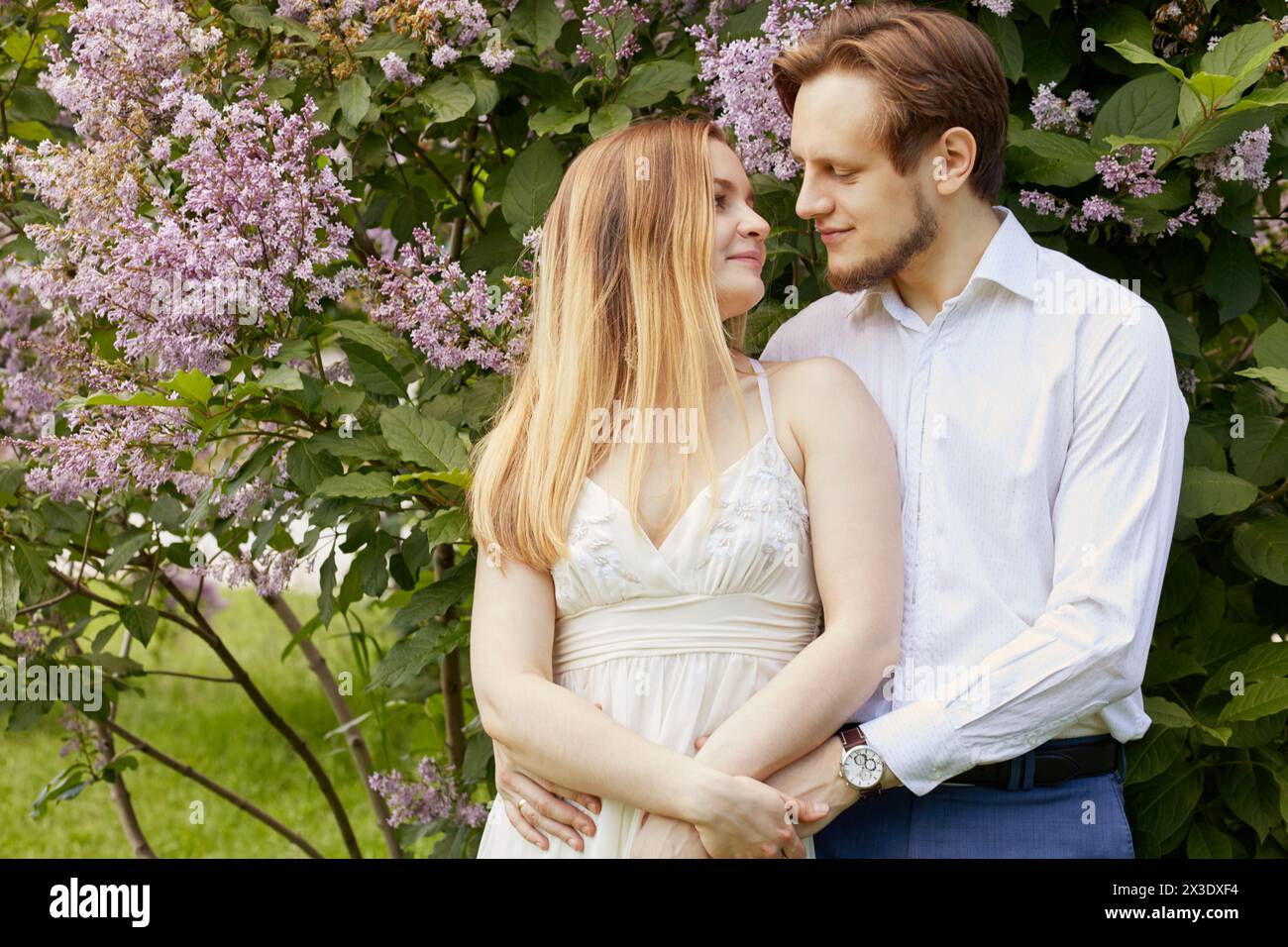 Young smiling bearded man and woman stand looking into eyes in park ...