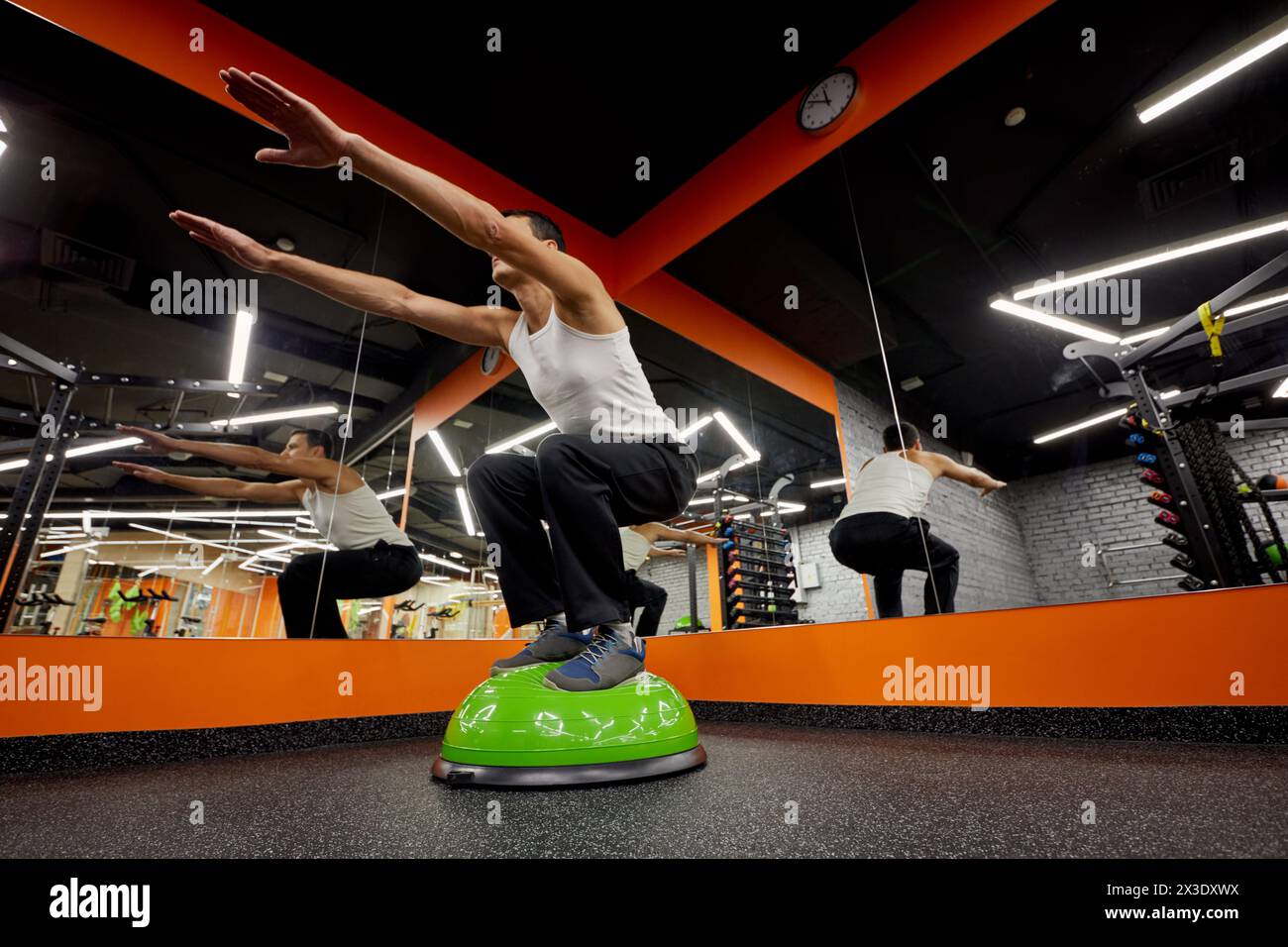 Man doing squatting exercises on inflatable semi ball at fitness studio ...