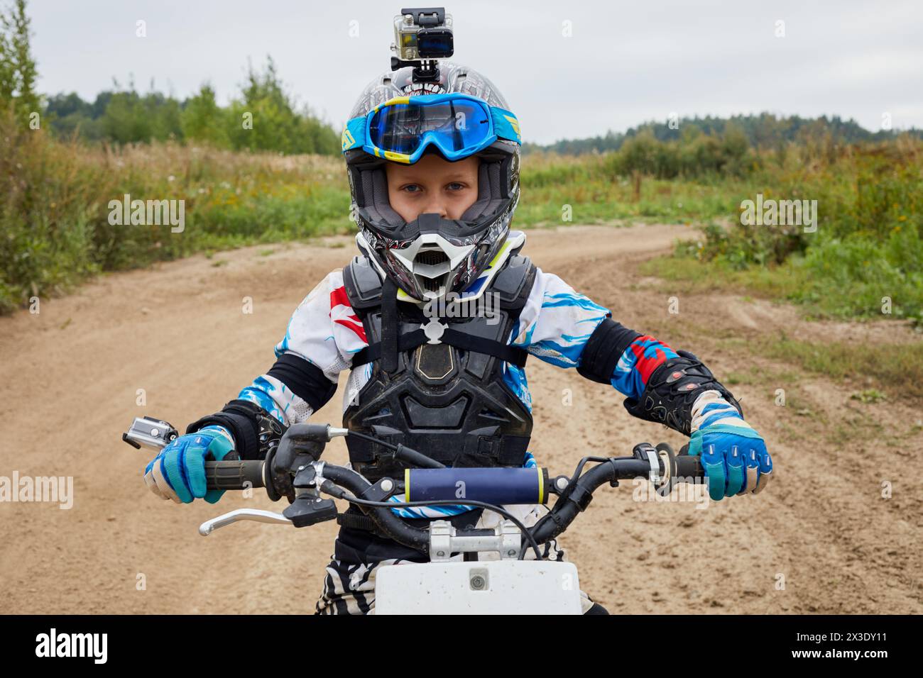 Portrait of boy dressed and equipped for motorbike racing sitting on ...