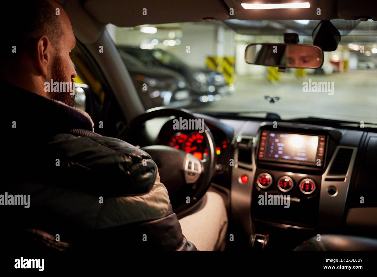 Bearded man sits on driver seat in car at underground parking, view ...