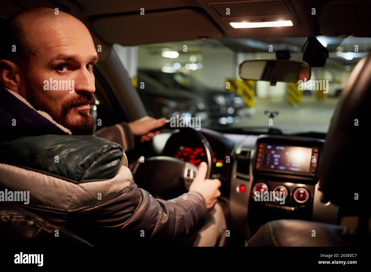Bearded man sits half-turned on driver seat in car at underground ...