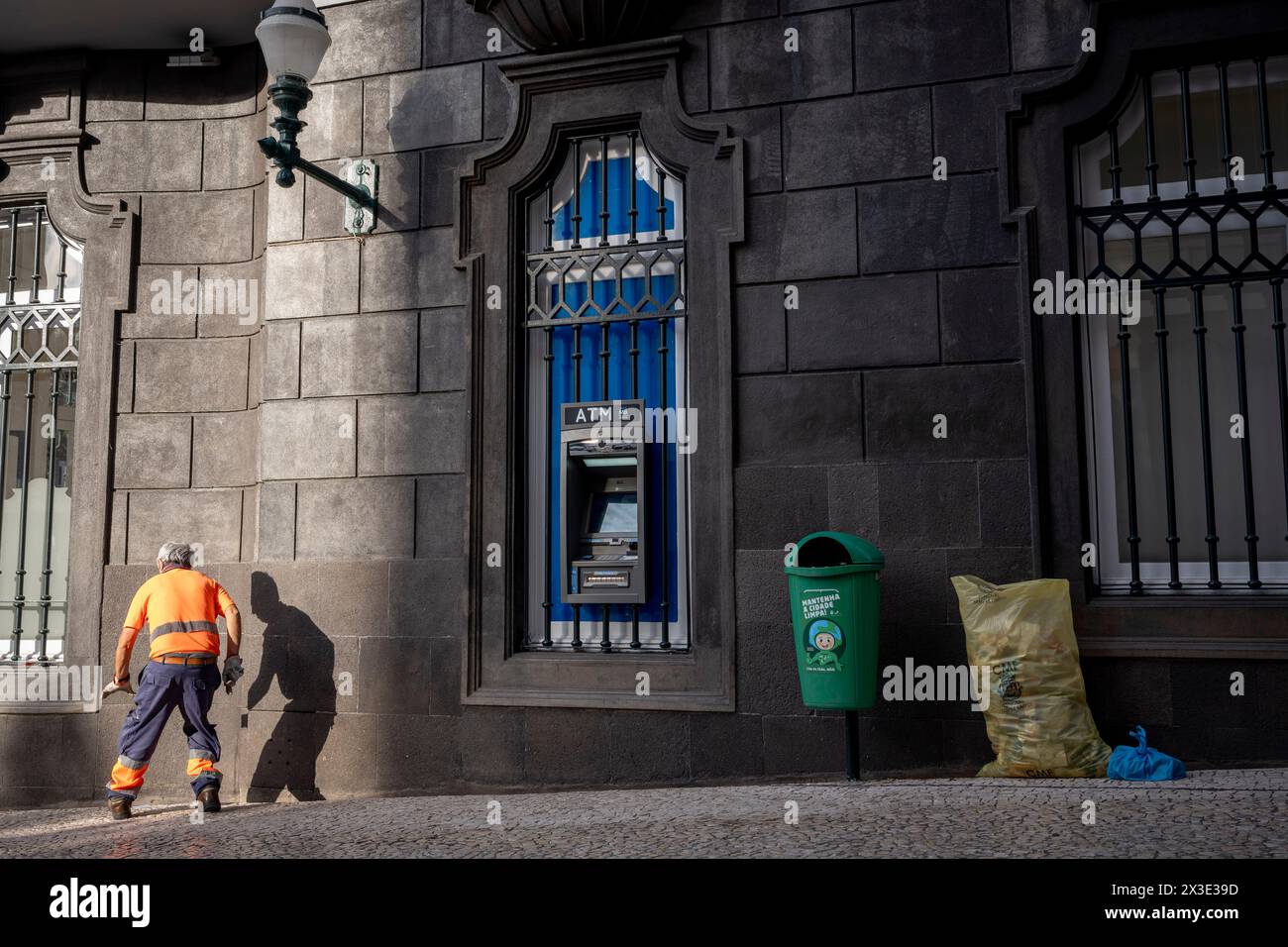A contractor removes litter and waste from the street by an ATM of ...