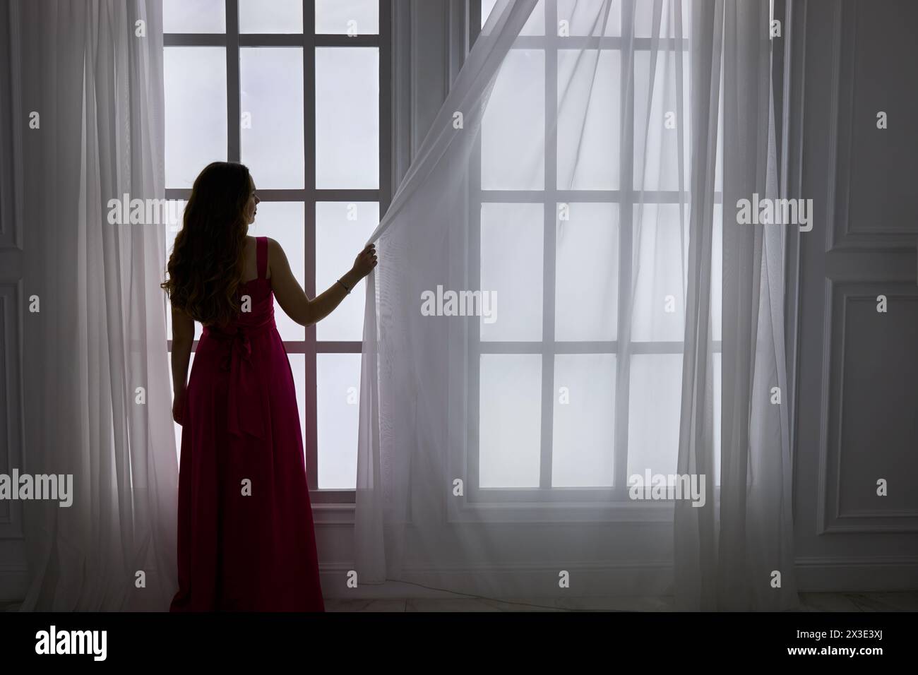 Young woman draws window curtain in dark room Stock Photo - Alamy