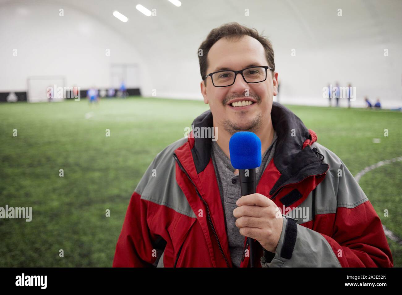 Smiling reporter with microphone on covered sports ground Stock Photo ...