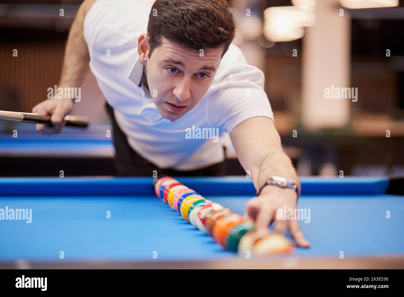 Man in white polo-neck shirt aligns balls in line on pool table Stock ...