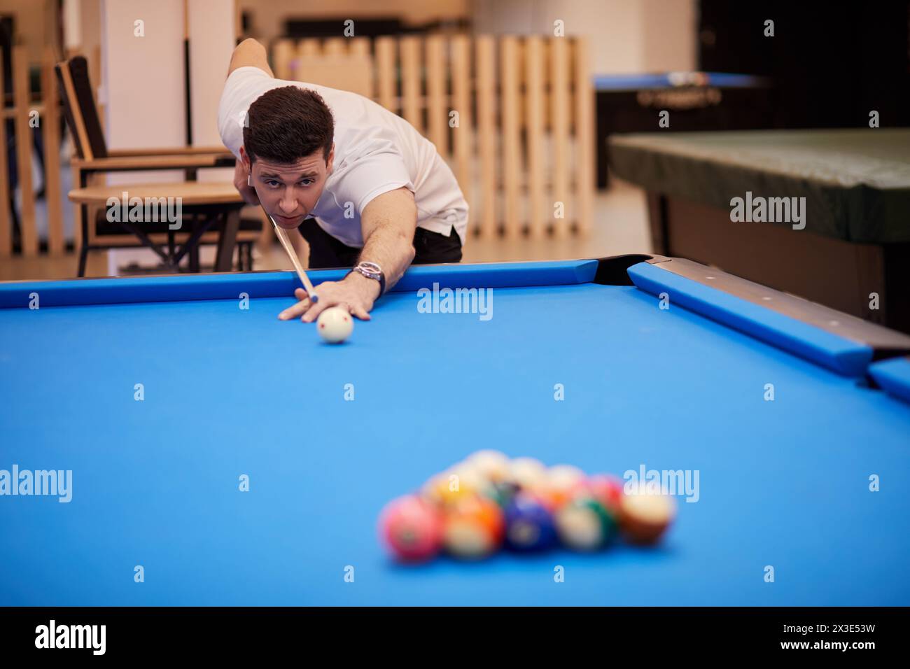 Man in white polo-neck shirt aims ball with cue stick on pool table in ...