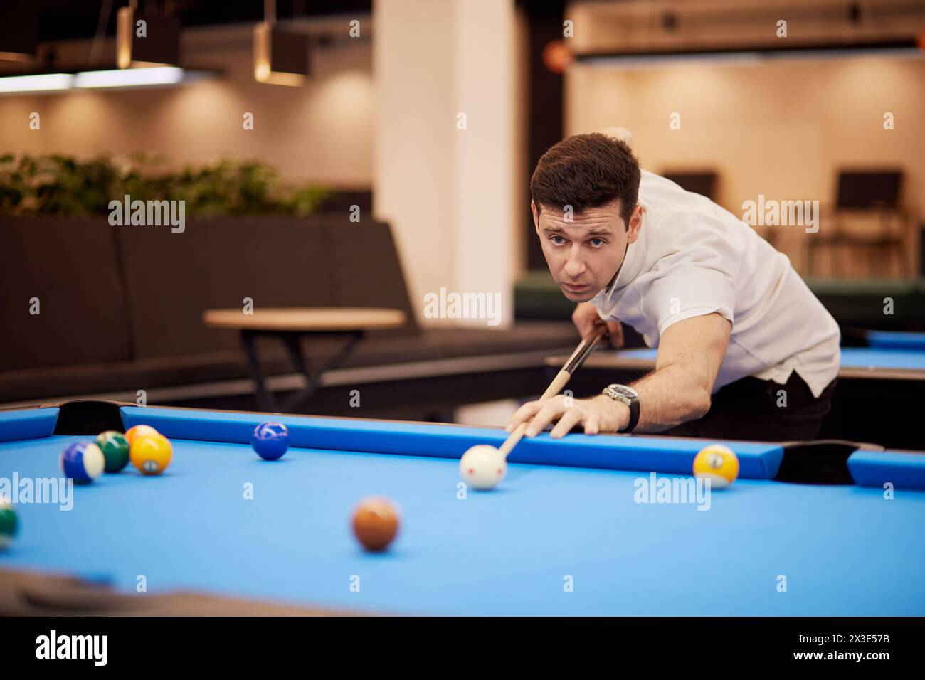 Man in white polo-neck shirt aims balls on pool table in club Stock ...