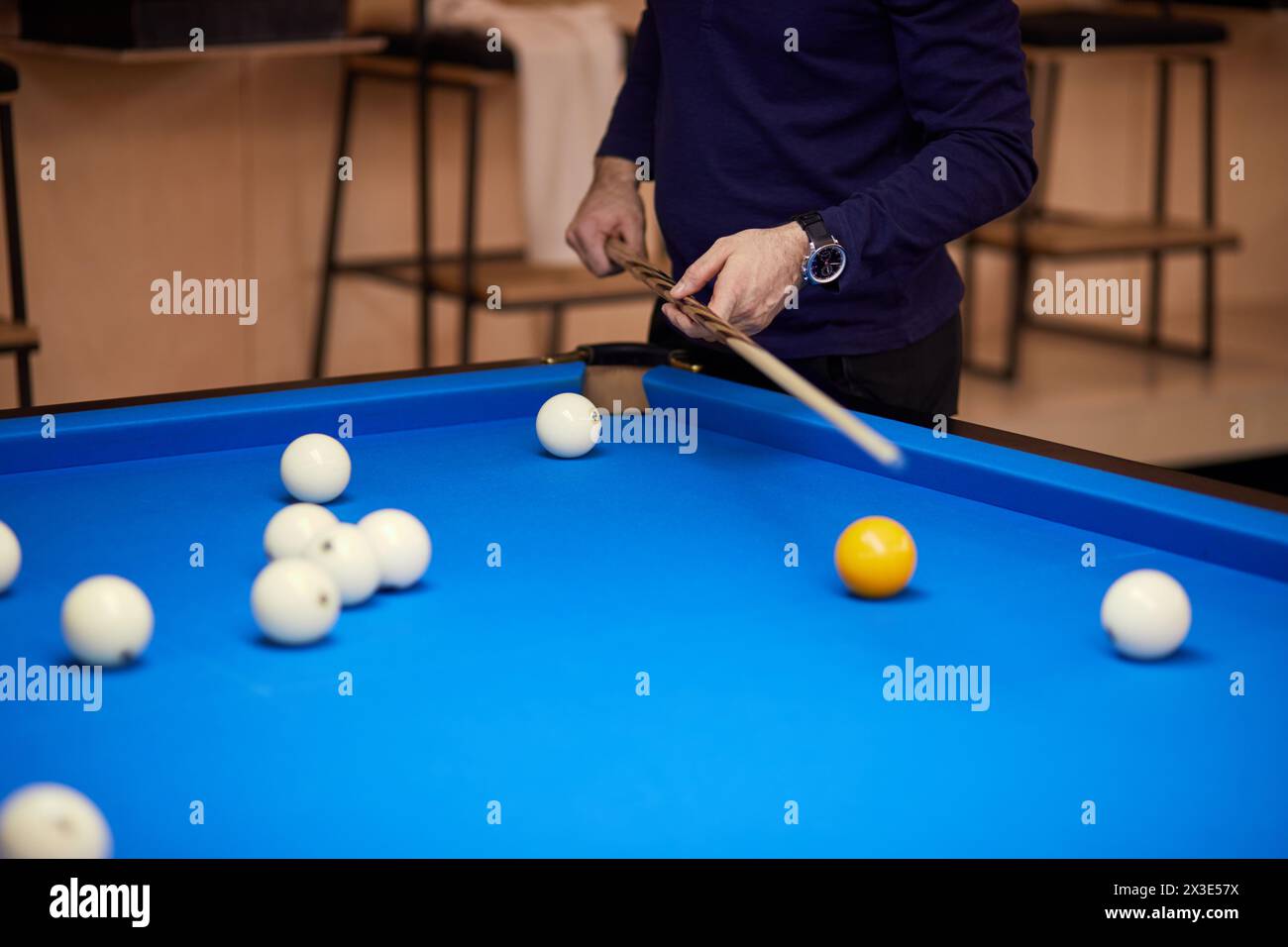 Man with cue stick in hands stands near pool table with balls in club ...