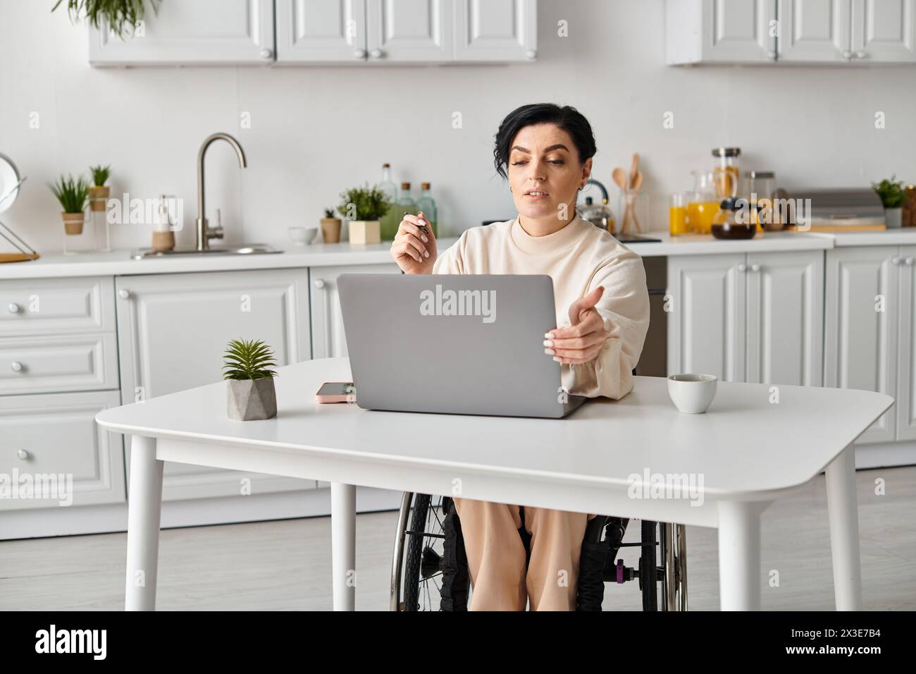 A disabled woman in a wheelchair is focused on her laptop at a kitchen ...