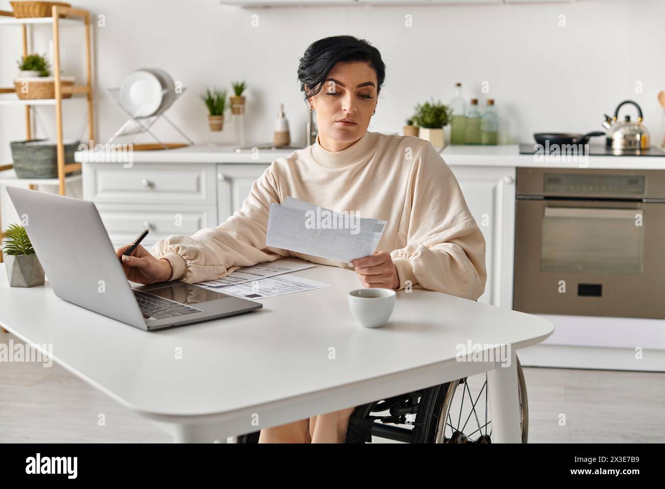 A disabled woman in a wheelchair works on her laptop at a kitchen table ...