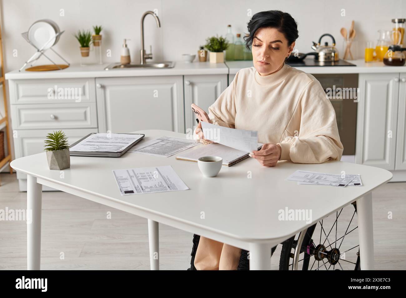 A disabled woman in a wheelchair sits at a kitchen table with papers ...