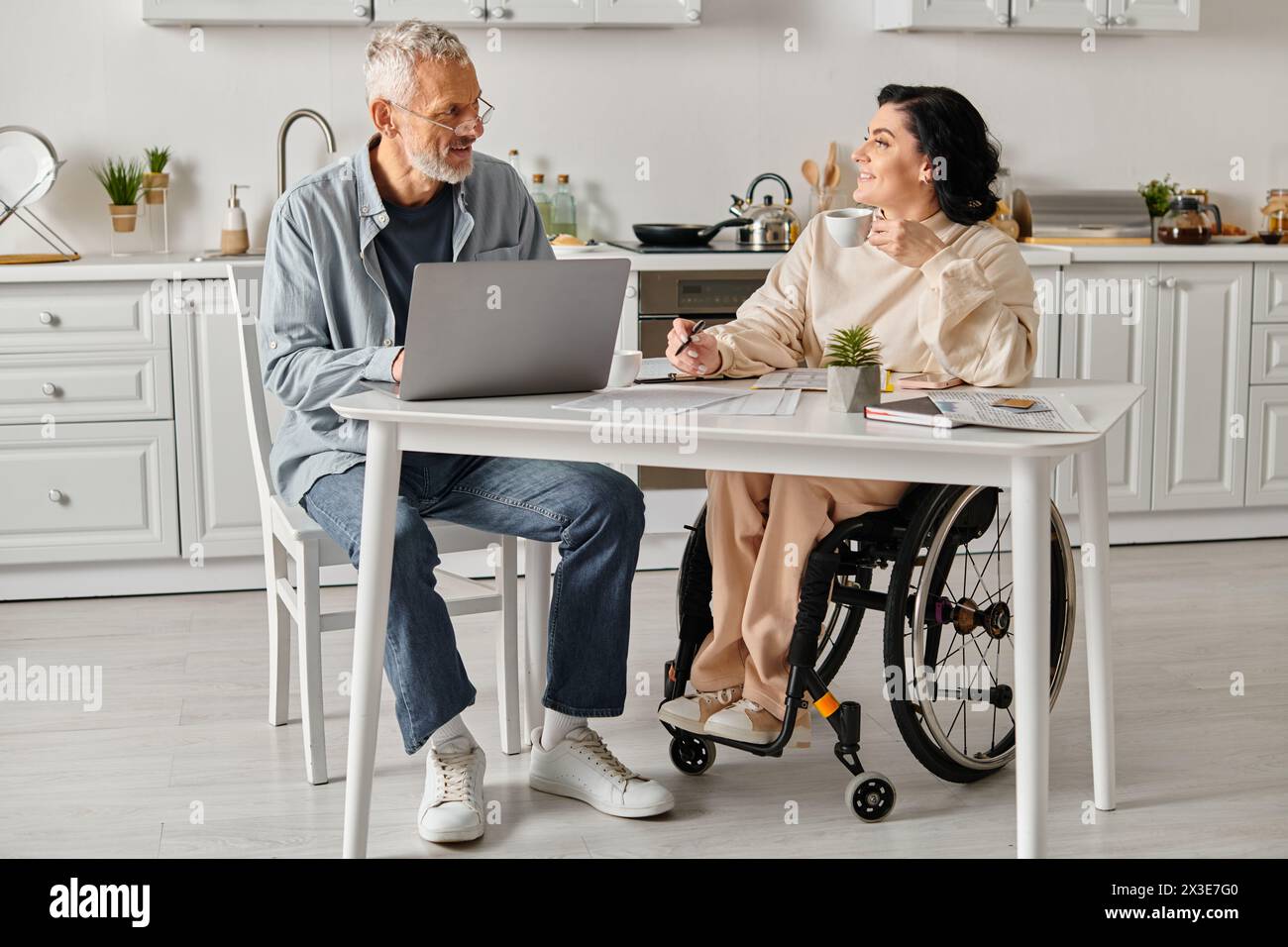 A husband and his disabled wife sit at a kitchen table working on a ...