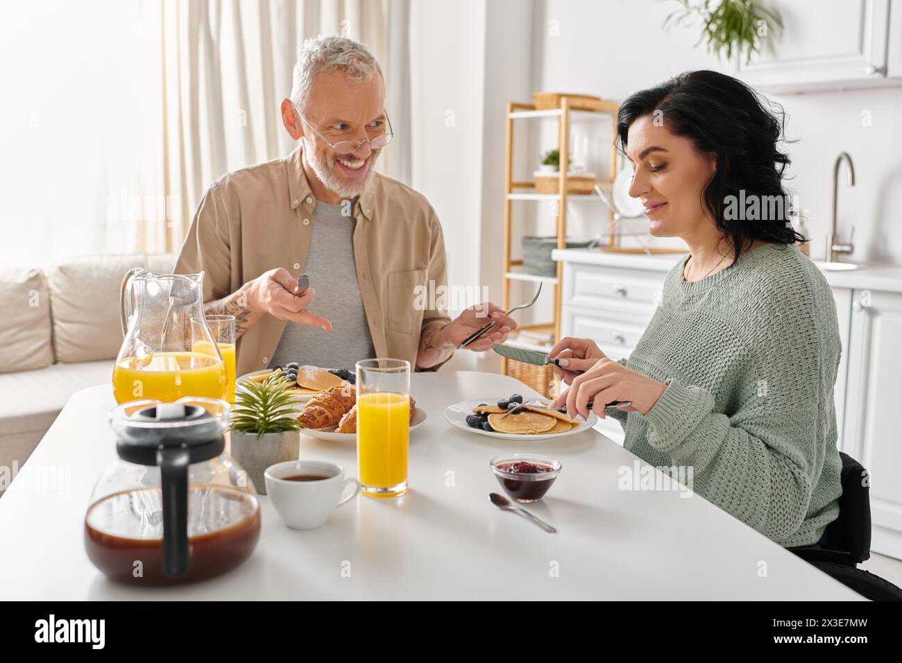 A man and disabled woman in a wheelchair share a meal at their kitchen ...