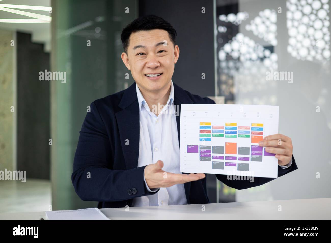 A cheerful Asian businessman presents a detailed colorful schedule ...