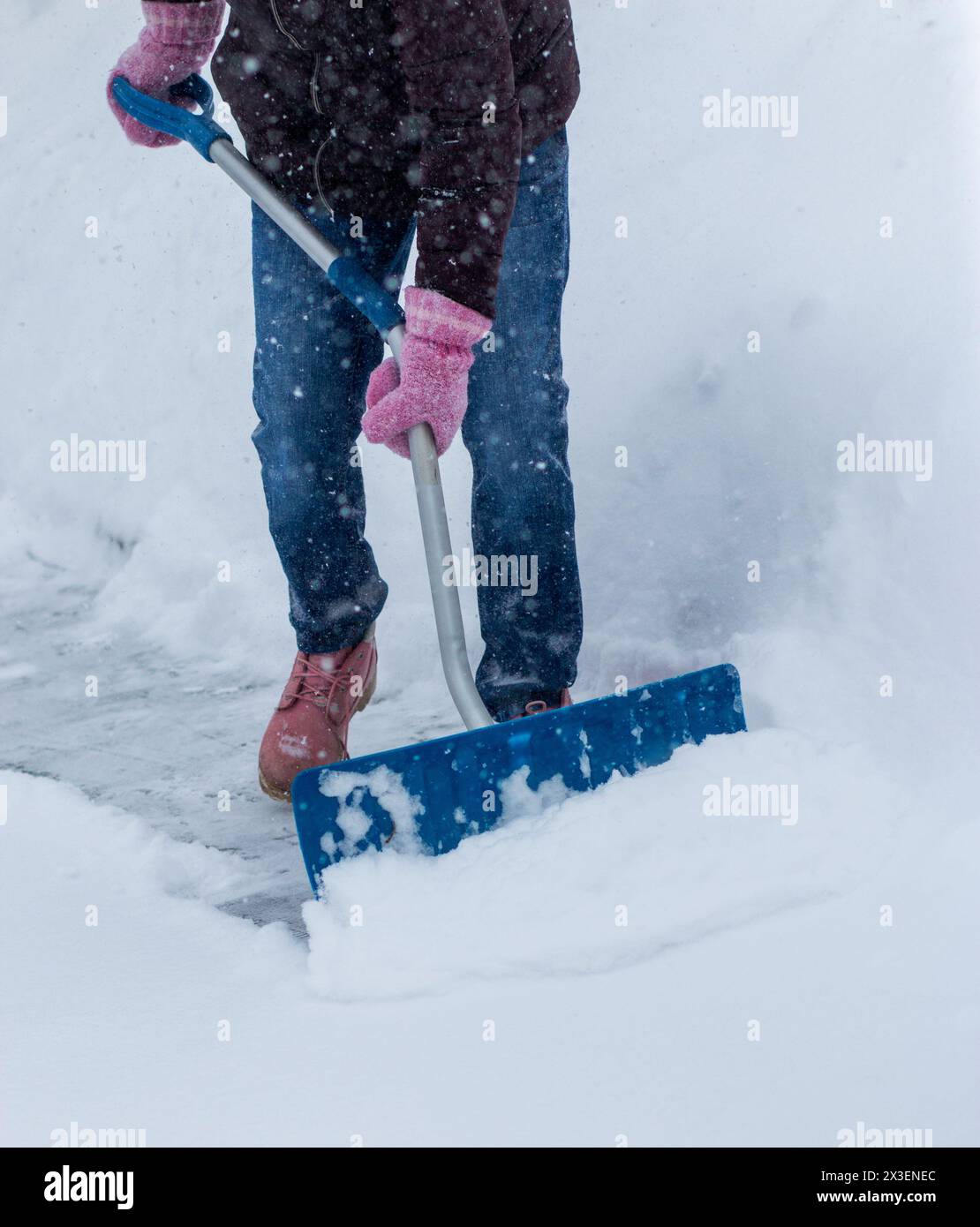 A woman is clearing snow from a sidewalk using a snow shovel. She is ...