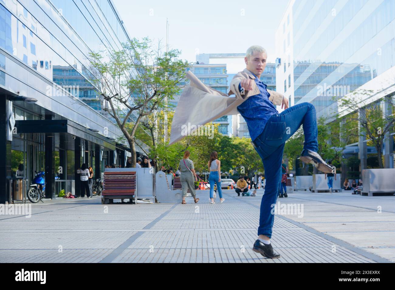 young gay man with short blonde hair, in profile on street jumping ...