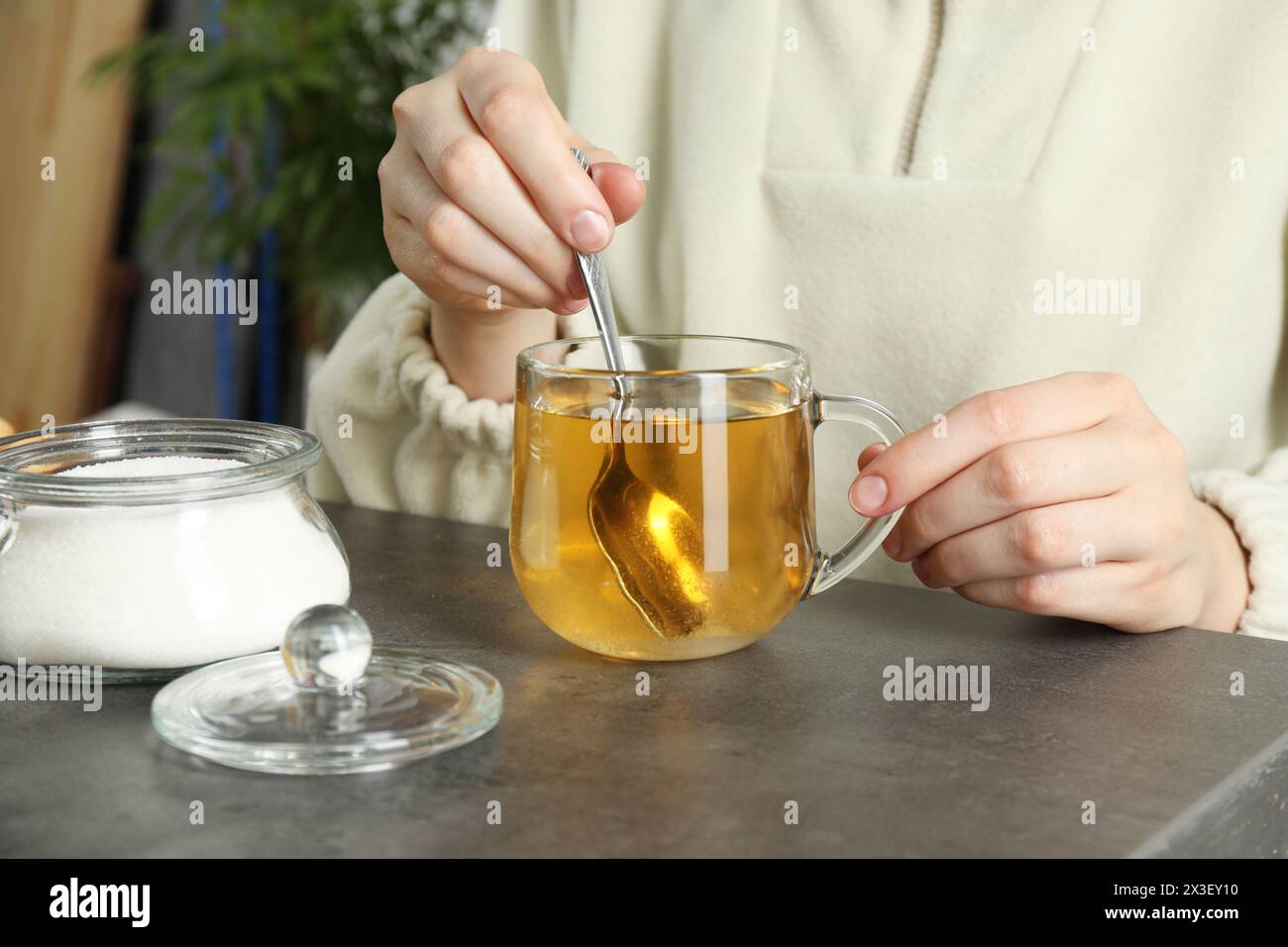 Woman stirring sugar in tea at grey table, closeup Stock Photo - Alamy