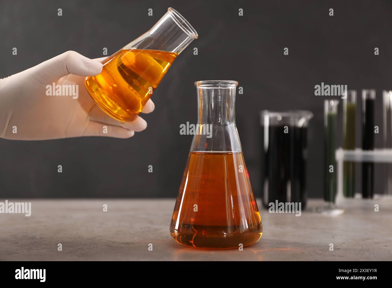 Woman pouring yellow crude oil into flask at grey table, closeup Stock ...