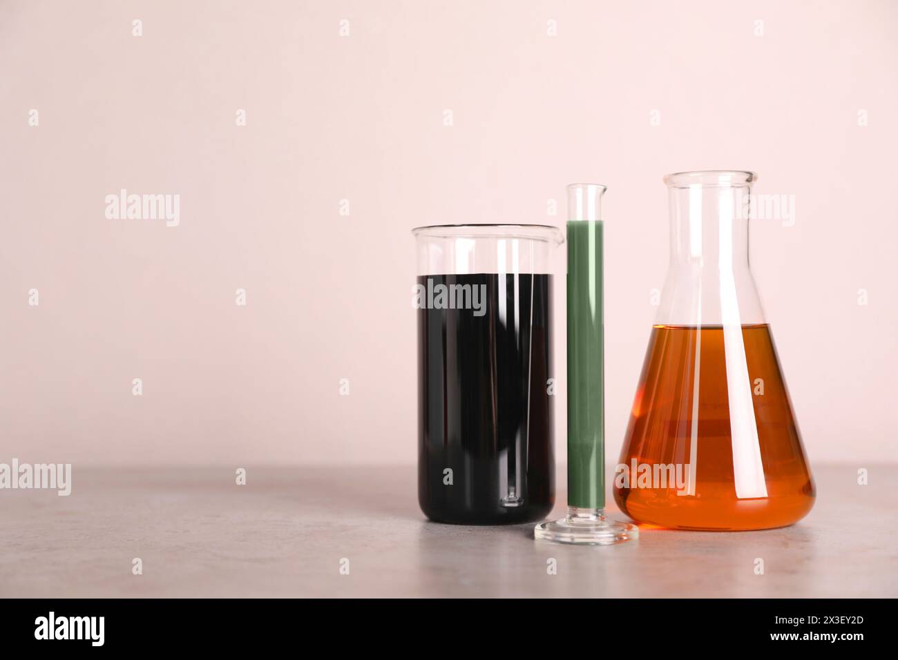 Test tube, beaker and flask with different types of oil on grey table ...