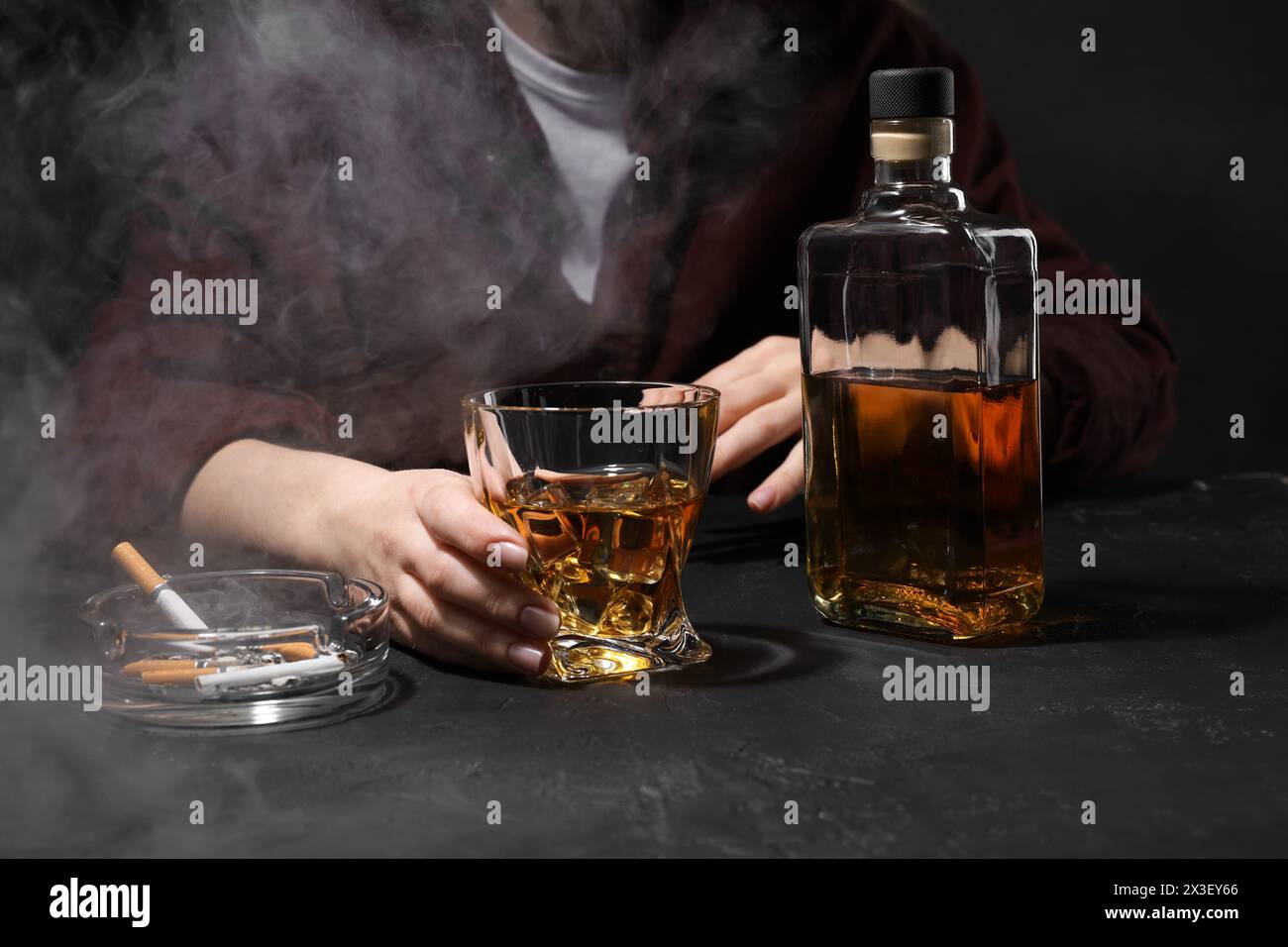 Alcohol addiction. Woman with whiskey and smoldering cigarettes at dark ...