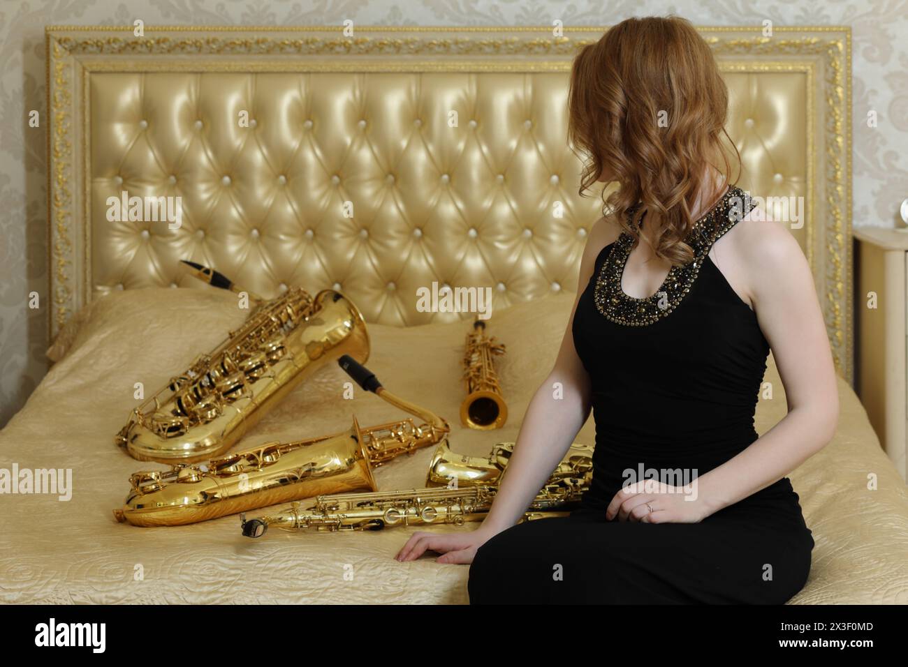 Woman in black dress sits with sax on bed with wind instruments in ...
