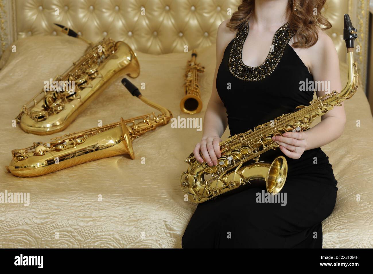 Woman in black dress sits with sax on bed with wind instruments, noface ...
