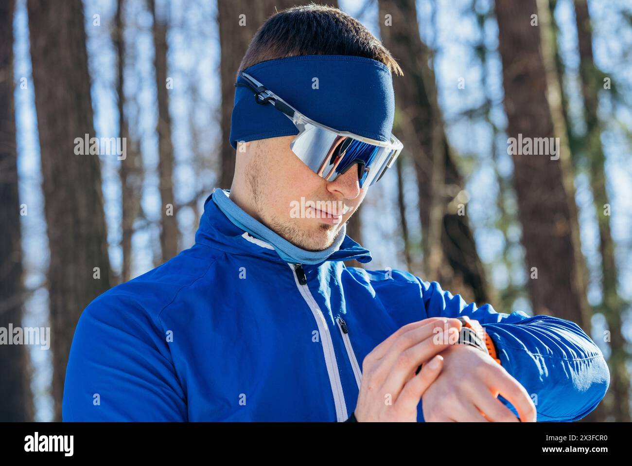 Focused male skier in a blue outfit and reflective goggles checks his ...