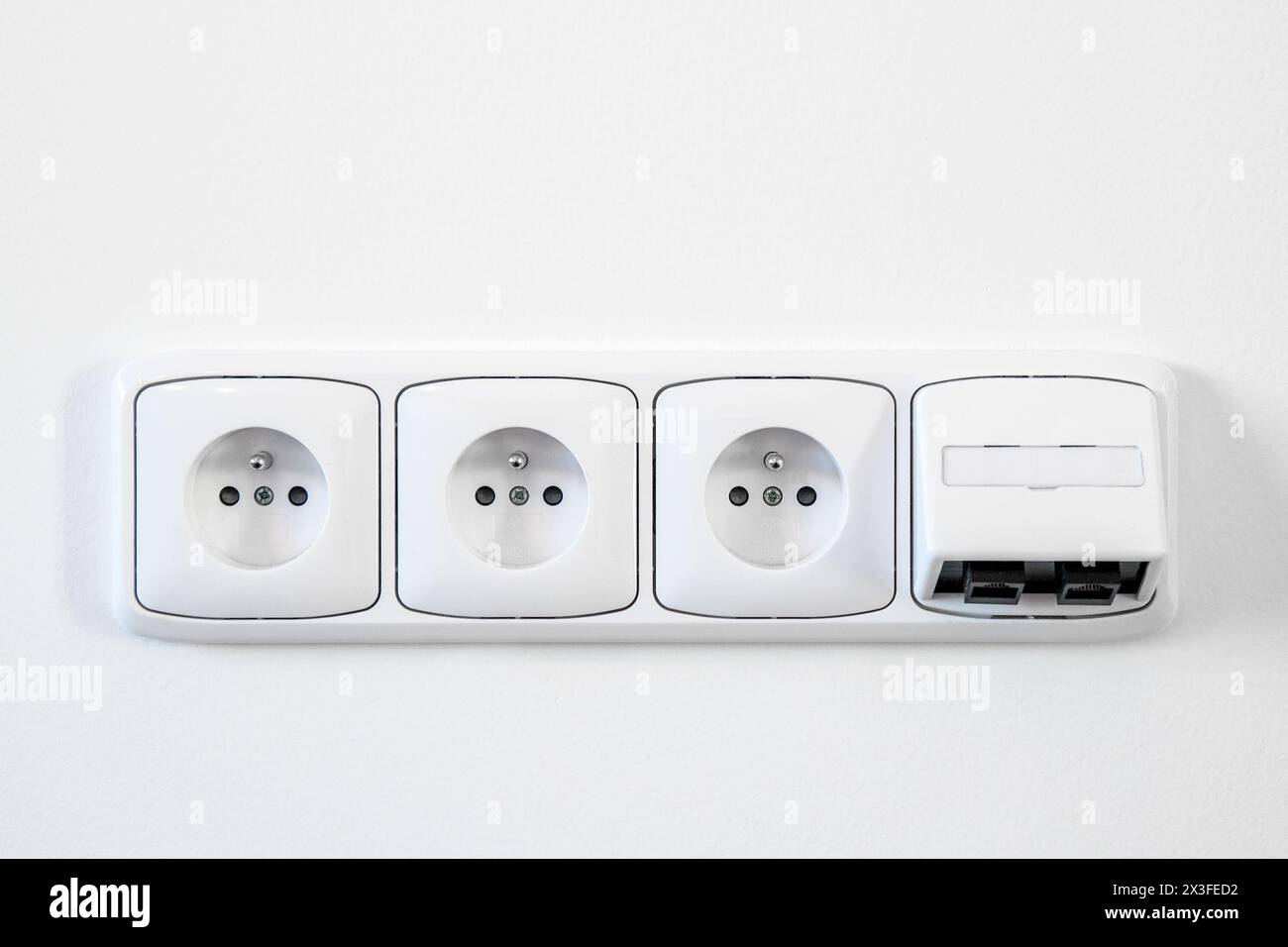 Three electricity plugs on a wall with two network RJ45 sockets for ...