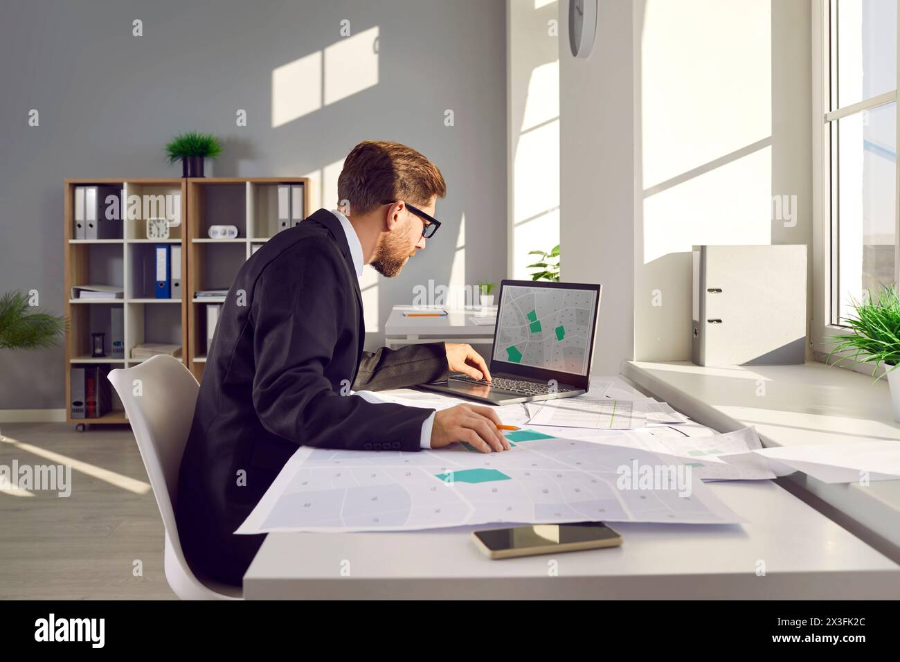 Cadastral surveyor sitting at office desk, working with cadastral maps ...