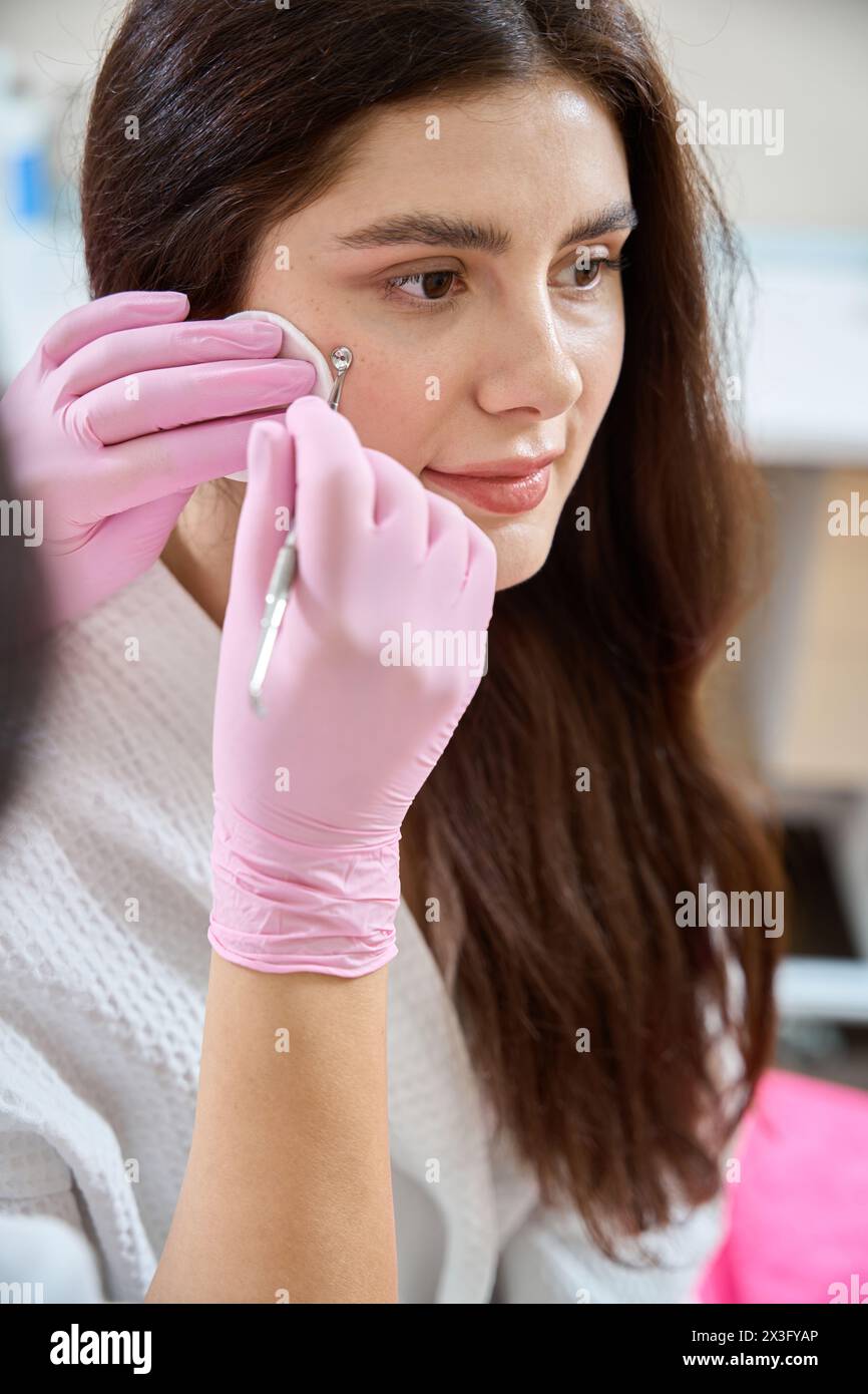 Cosmetician carrying out comedone extraction on young female client ...