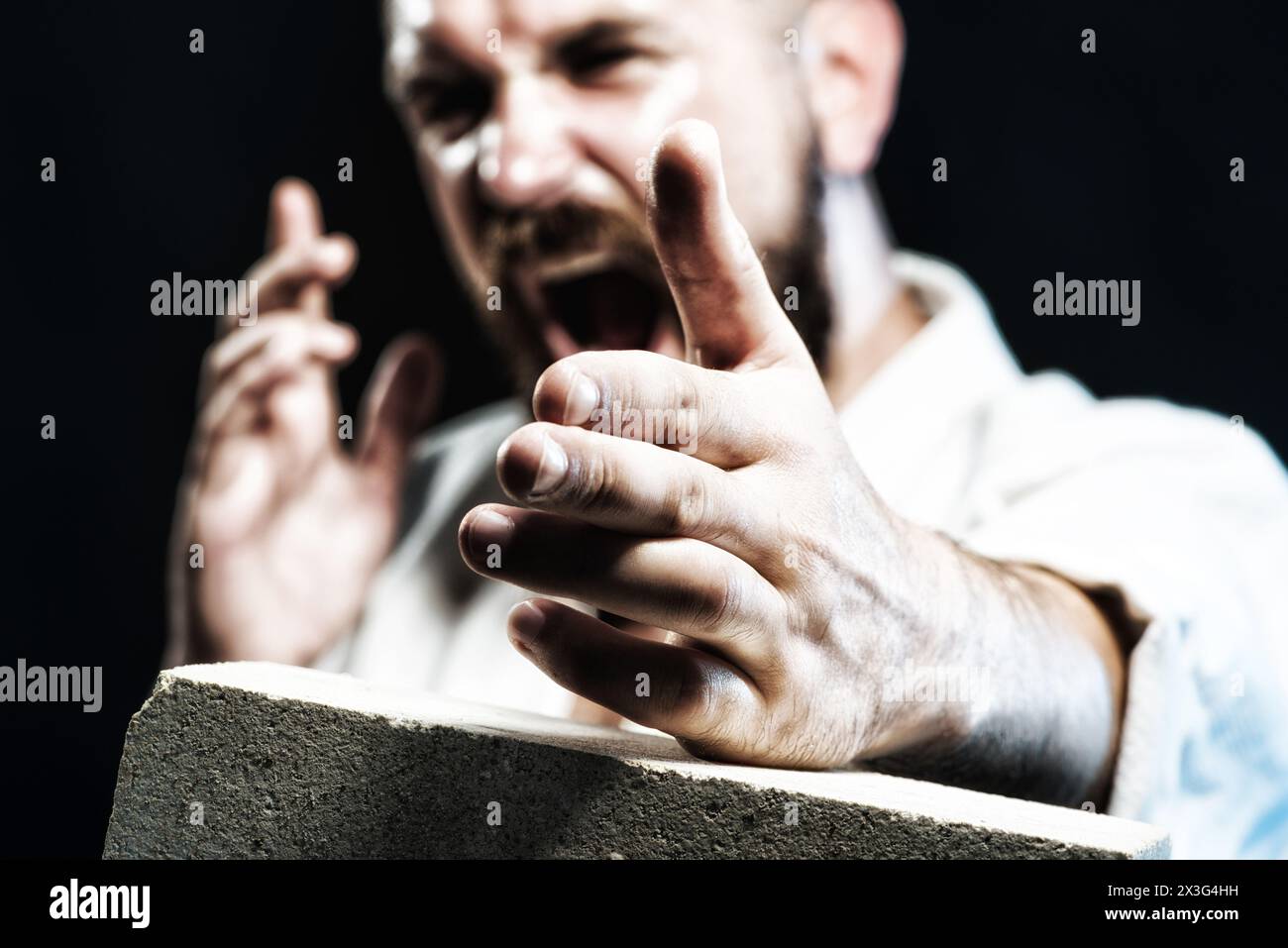 Bearded screaming karate man breaking with hand concrete brick. Mixed ...