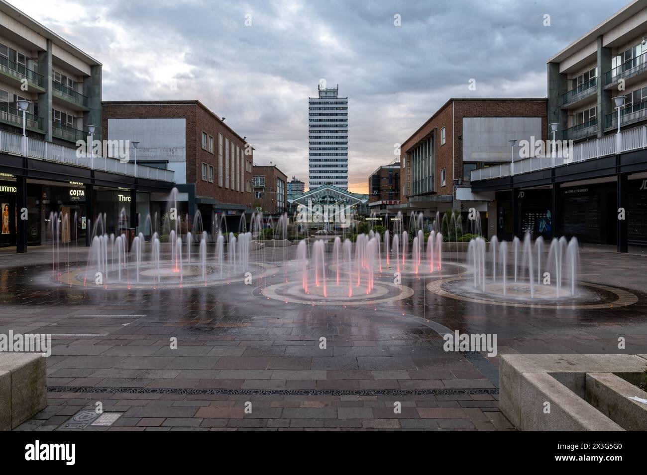 Illuminated fountains in a modern city square with buildings at dusk ...