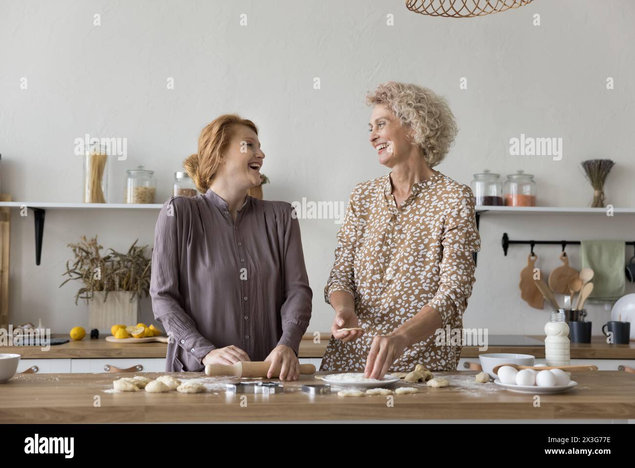 Woman and grownup daughter talking laughing while cooking in kitchen ...