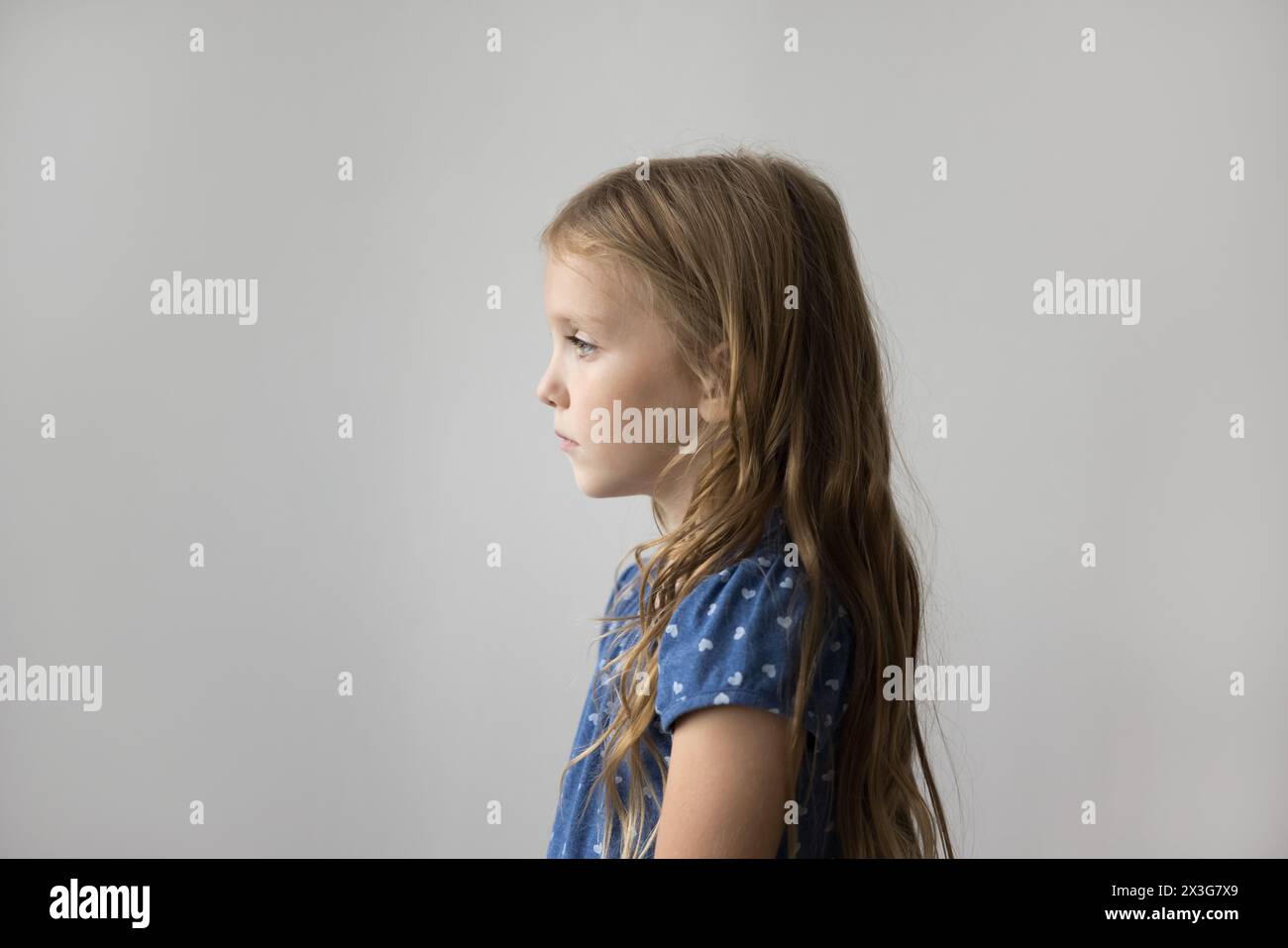 Side view serious little girl standing against gray studio background ...