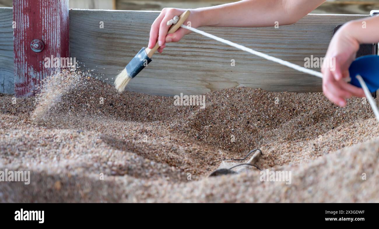 Child brushing away sand at a dinosaur fossil dig exhibit Stock Photo ...