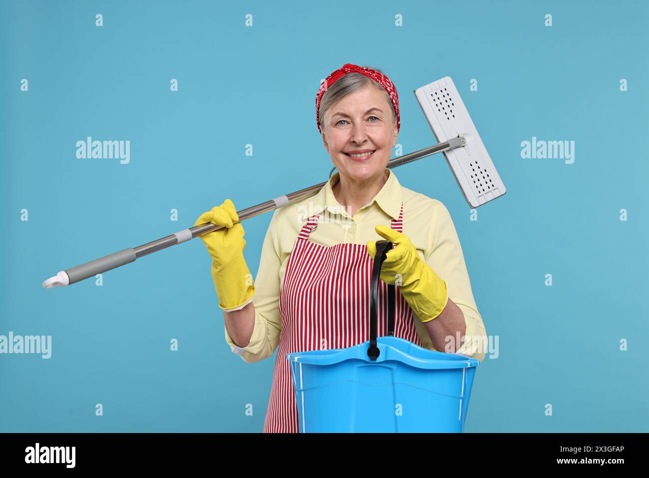 Happy housewife with mop and bucket on light blue background Stock ...