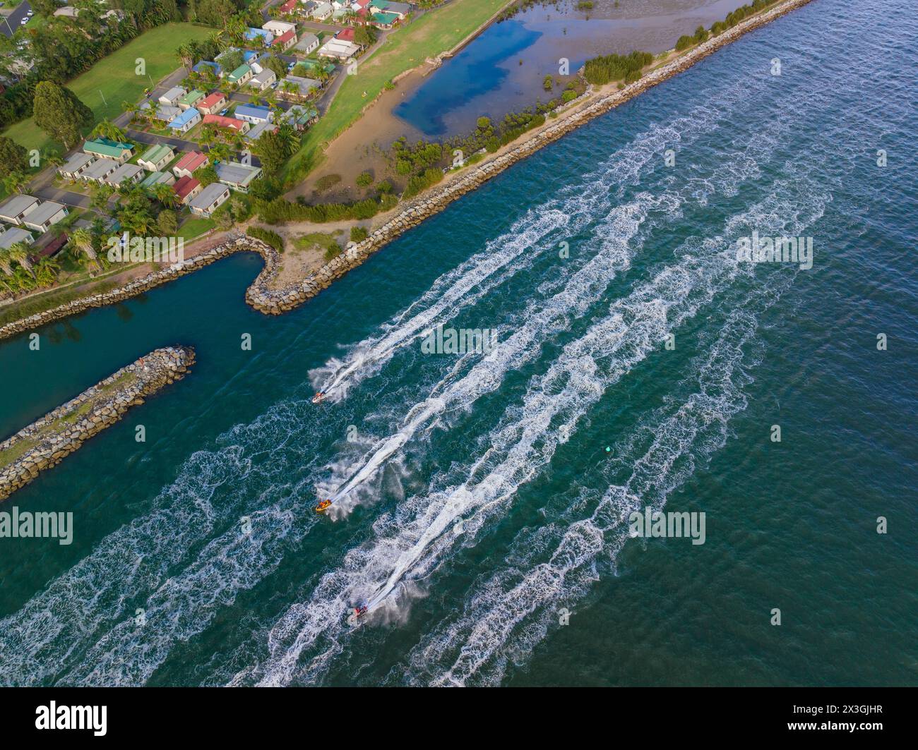 Aerial view of jet skis creating long wakes alongside coastal ...