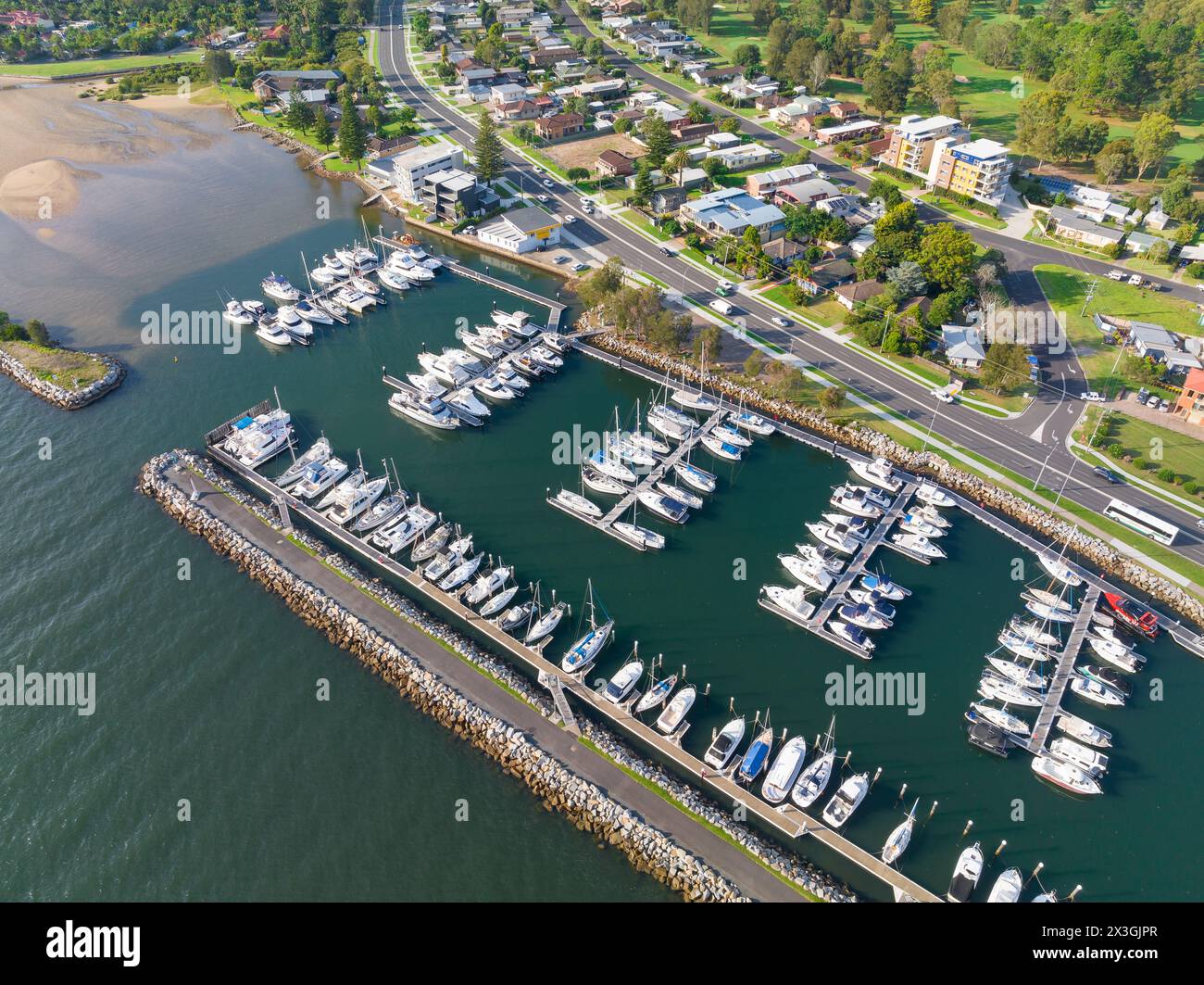 Aerial view of lines of boats at a coastal marina alongside a busy road ...