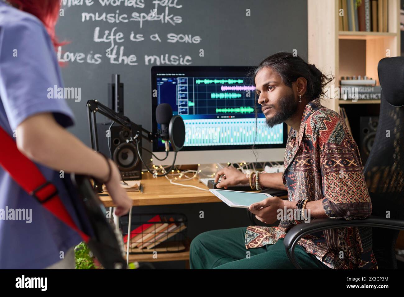 Serious male musician sitting by workplace and adjusting sound of ...