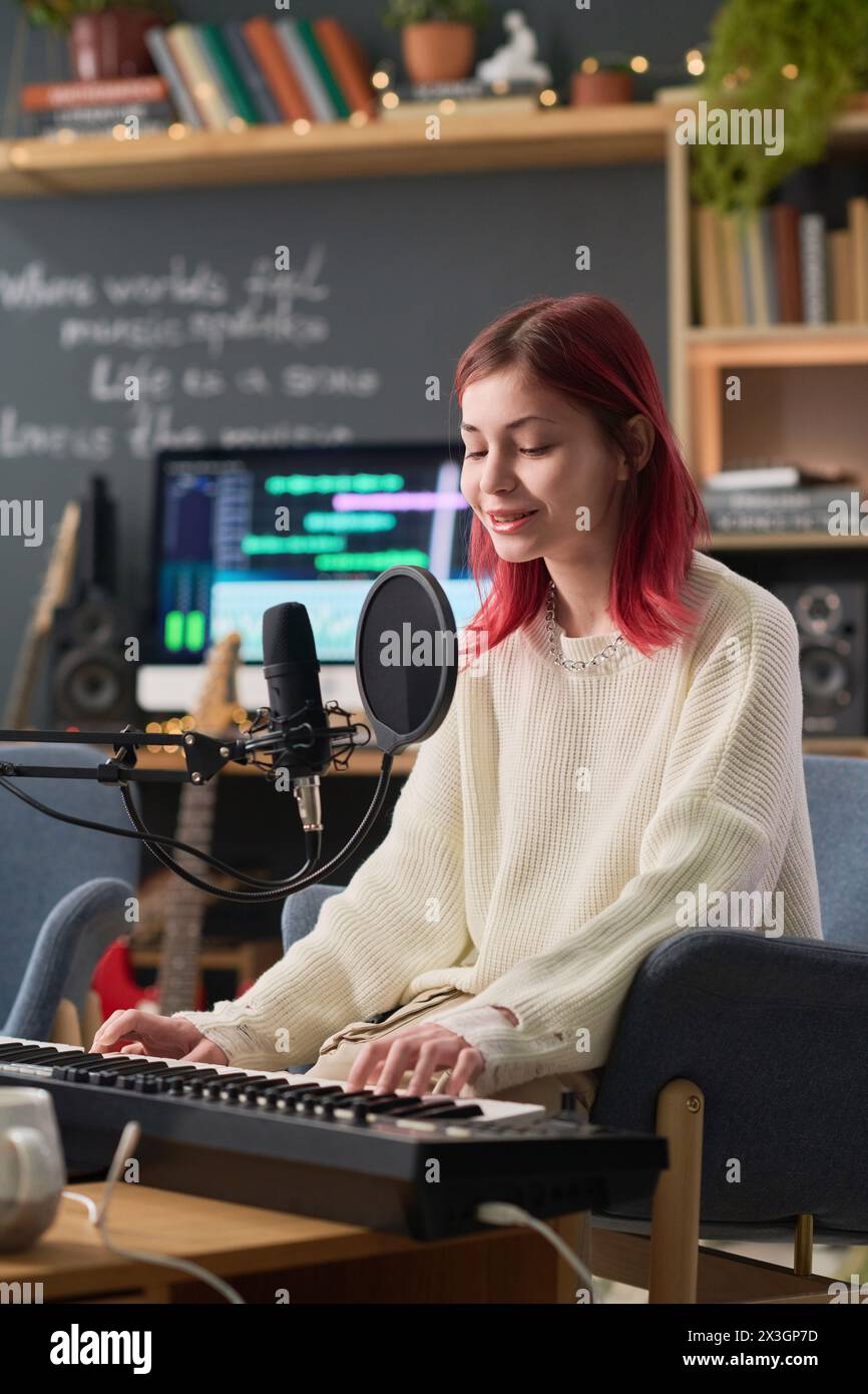 Smiling female teenager in white sweater pressing keys of electric ...