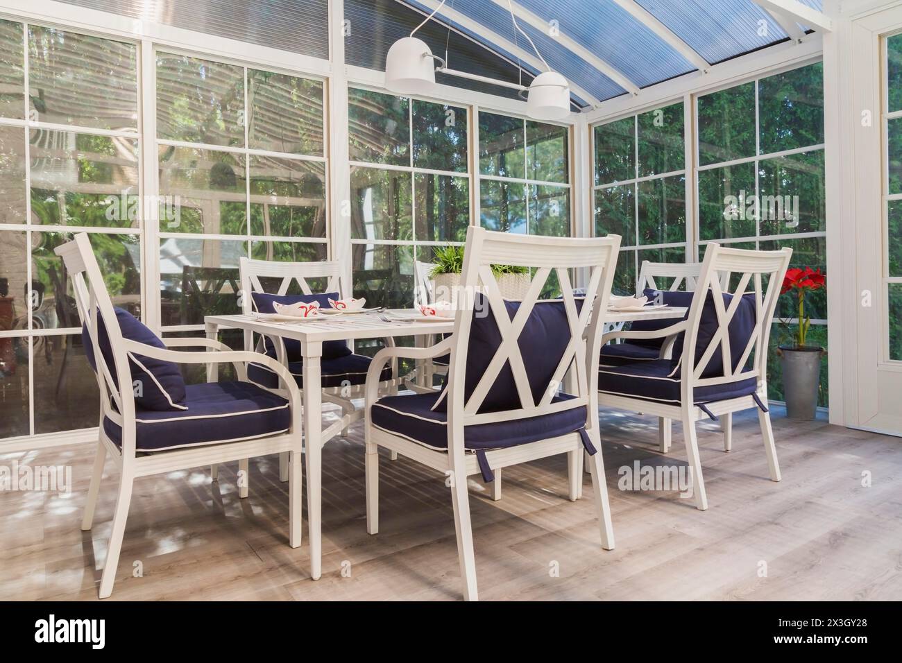 White dining table and armchairs with blue cushions in sunroom at back ...