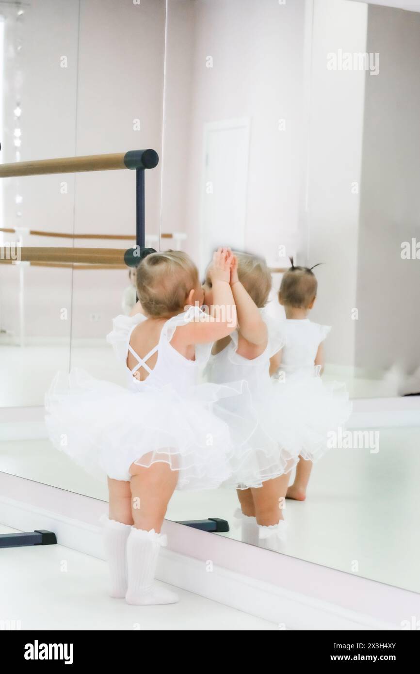 Portrait of a cute baby ballerina sitting near the ballet barre putting ...